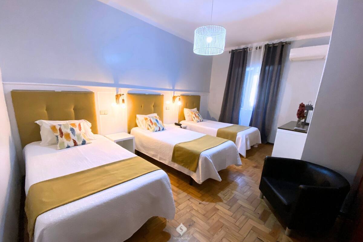 Quarto de hotel com duas camas, uma escrivaninha, uma cadeira e um candelabro.