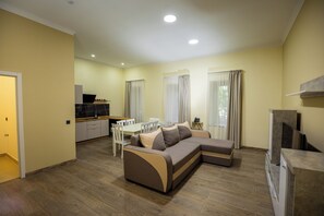 Sala de estar com sofá seccional, mesa de jantar, cadeiras, área de cozinha e televisão.