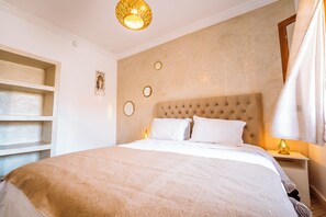 Quarto com cabeceira estofada, luminária de cabeceira e estante.
