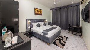 Quarto de hotel com cama, escrivaninha, cadeira, televisão e ventoinha no teto.