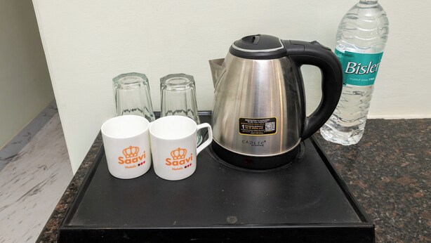 Máquina de café, duas canecas com a marca e uma garrafa de água em uma bancada.