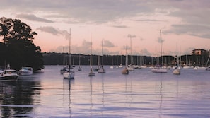 Uma marina com vários veleiros atracados, águas calmas e um cenário de árvores e edifícios.