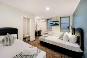 Quarto de hotel com duas camas, uma escrivaninha, uma cadeira, uma televisão e um banheiro.
