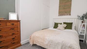 Quarto com cama, penteadeira, radiador branco e tapeçaria na parede.