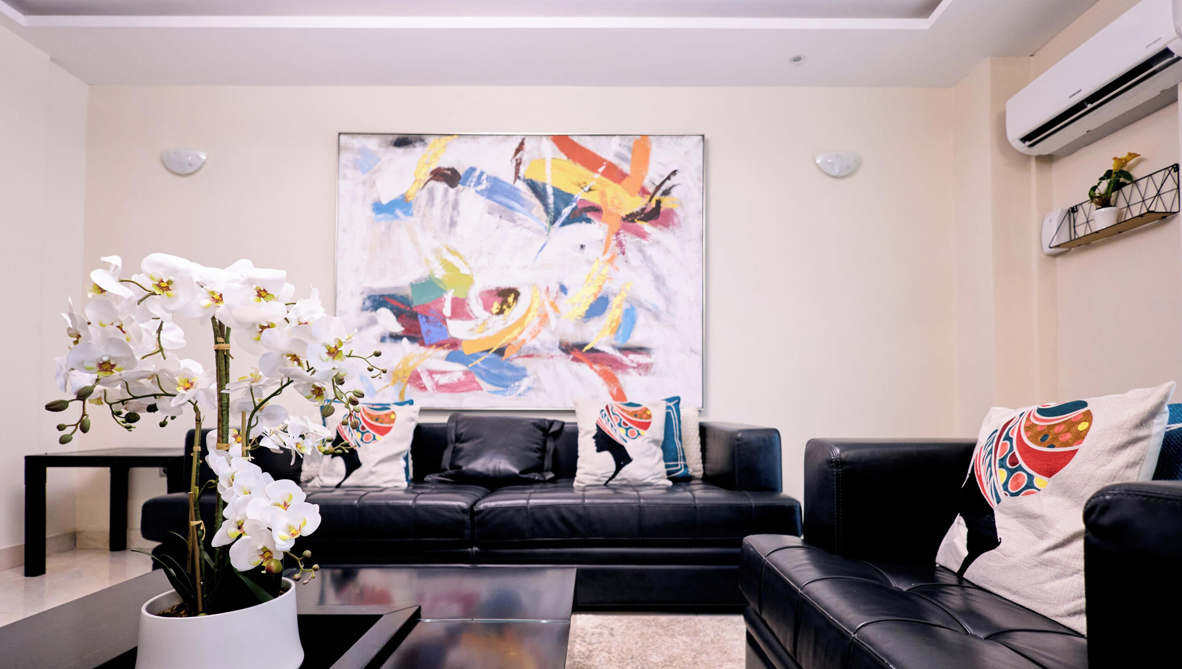 Uma sala de estar moderna com um sofá de couro preto, uma mesa de centro e um grande quadro abstrato na parede.