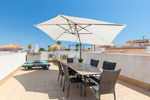 Terraço no telhado com mesa, cadeiras e um grande guarda-sol, com um carro estacionado perto.