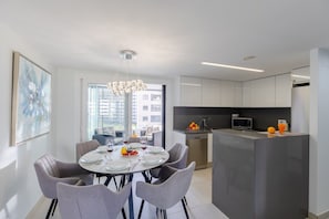 Cozinha moderna com área de jantar, apresentando uma mesa redonda com cadeiras, uma ilha integrada e uma grande janela com vista para a cidade.