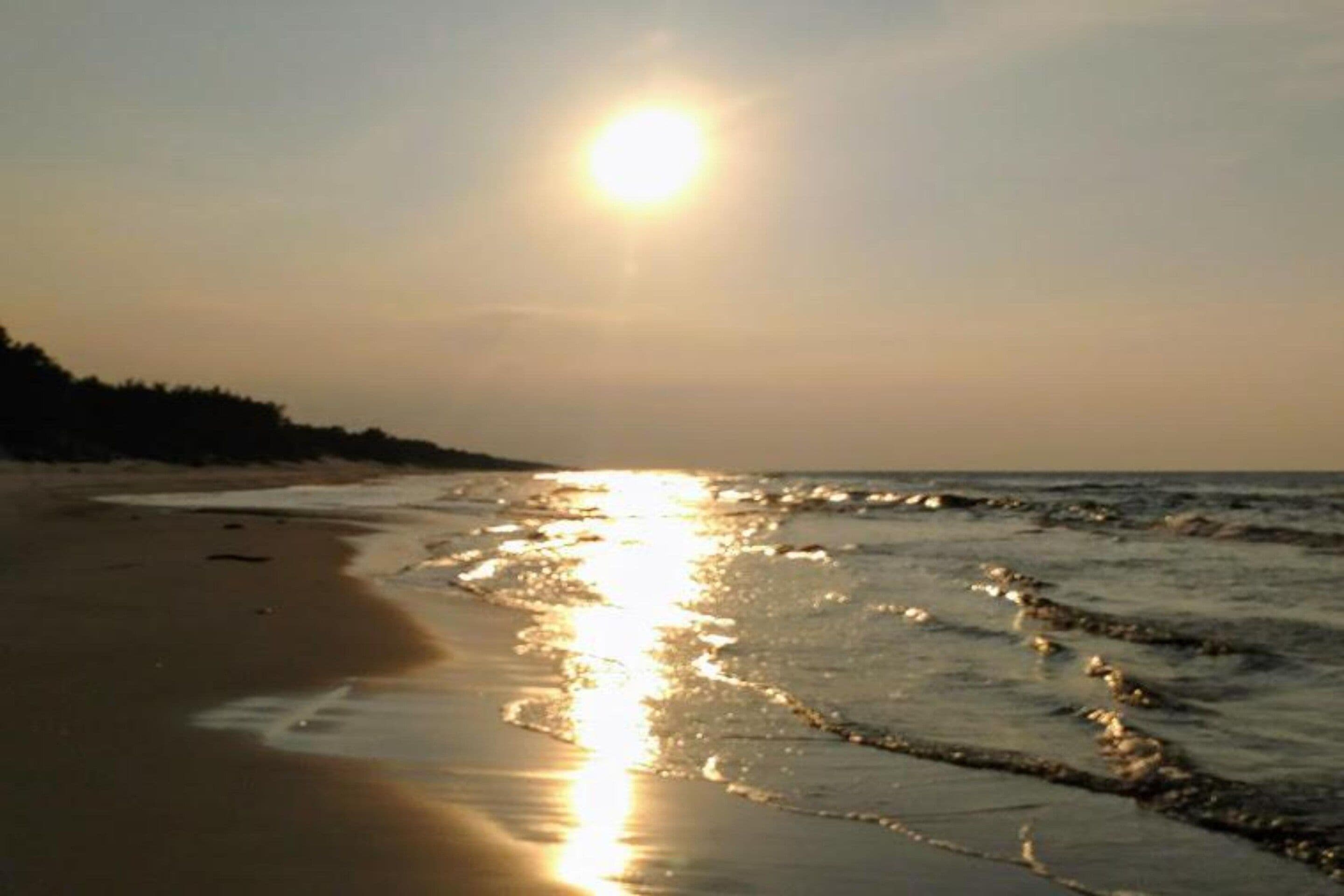 Uma praia com o sol baixo no horizonte, refletindo na água.