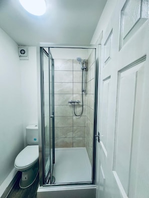Um chuveiro pequeno e fechado, com porta de vidro, vaso sanitário e um respiradouro fixado na parede.