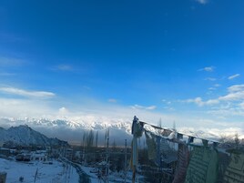 Paisagem montanhosa com picos nevados, céu claro e vista de uma aldeia com edifícios e linhas de energia.
