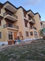 Um edifício residencial com várias andares, varandas, entrada principal e um pequeno jardim.