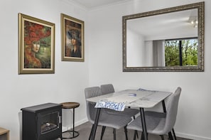 Uma sala de jantar com mesa, cadeiras, lareira e duas pinturas emolduradas na parede.