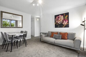 Uma sala de estar moderna com área de jantar, um sofá cinzento, um quadro e um abajur.