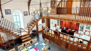 Uma sala de jantar ampla, com pé direito alto e escada que dá acesso a um andar superior.