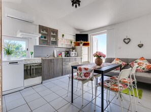 Cozinha moderna com área de refeições, eletrodomésticos brancos e sofá cinza.