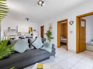 Uma sala de estar moderna com um sofá cinza, uma mesa de centro e uma cozinha ao fundo.