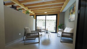 Uma sala de estar espaçosa com teto alto, vigas de madeira embutidas, porta de vidro deslizante que dá para uma varanda e móveis modernos.