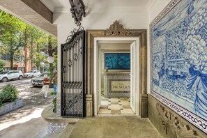 A entrada de um edifício com um muro de azulejos, um portão e vista para carros estacionados.