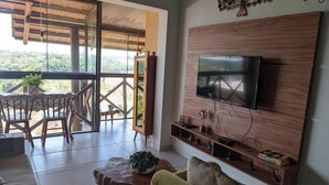 Uma sala de estar moderna com televisão, painel de parede em madeira e uma varanda com cadeiras e uma mesa.