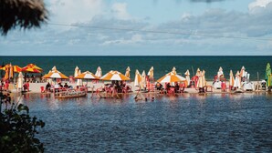 Uma praia com guarda-sóis e cadeiras, um barco e o oceano.
