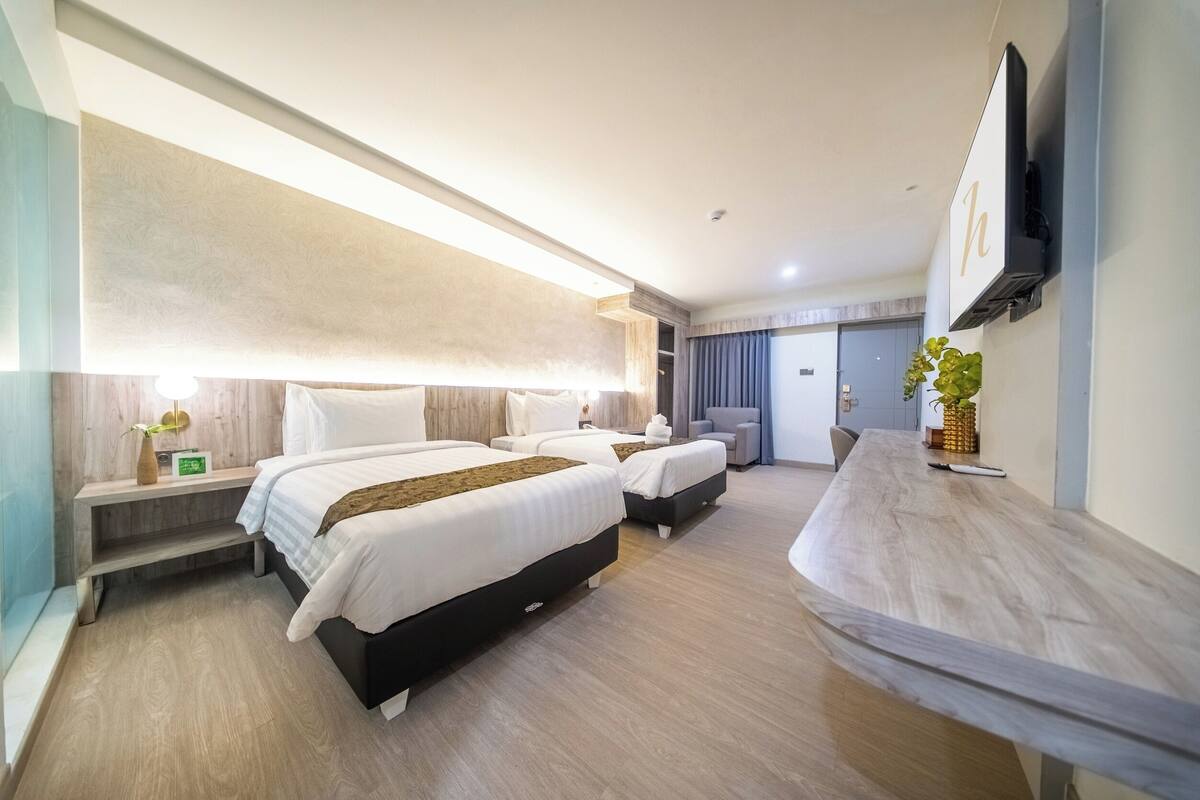Quarto de hotel com duas camas, uma escrivaninha, televisão e uma planta.
