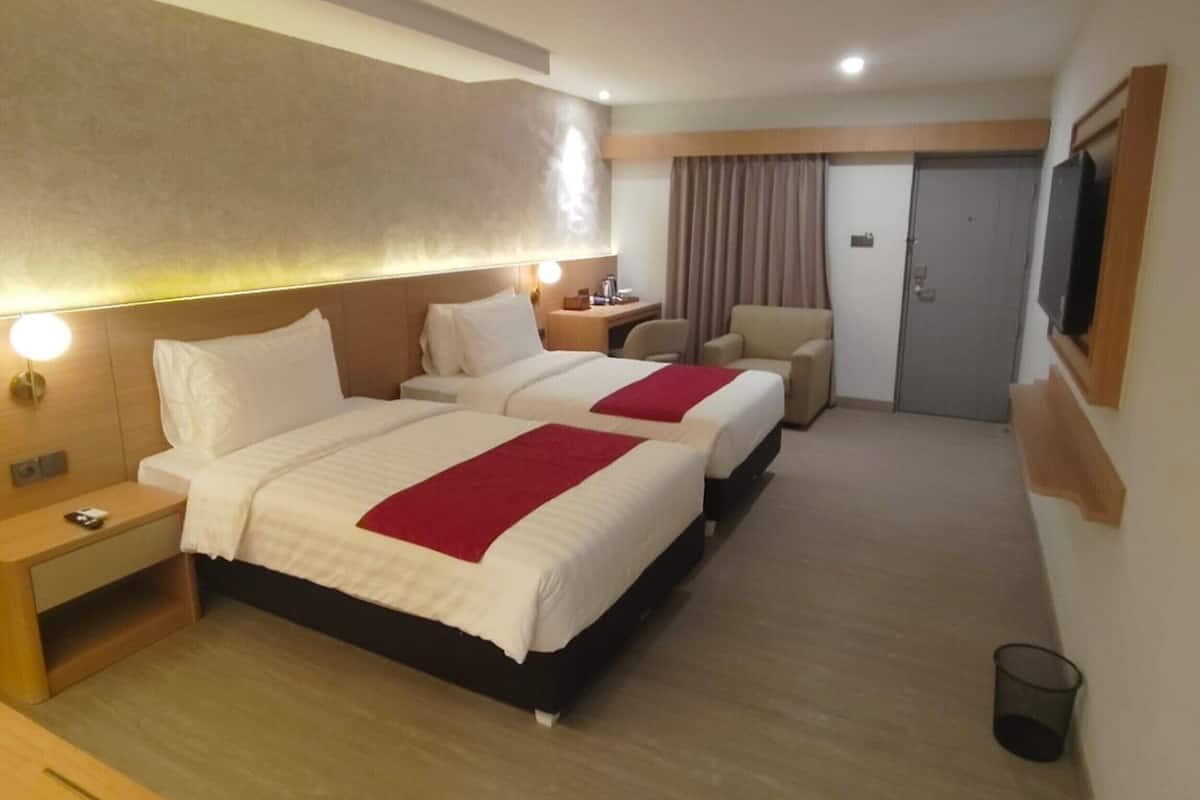 Quarto de hotel com duas camas, uma escrivaninha, uma cadeira, uma TV e uma porta.