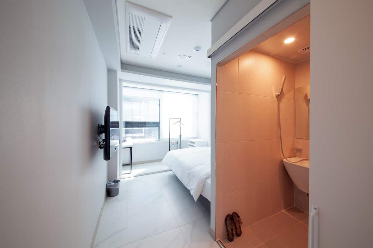 Quarto de hotel moderno com cama, secretária, chuveiro e vista para a cidade.