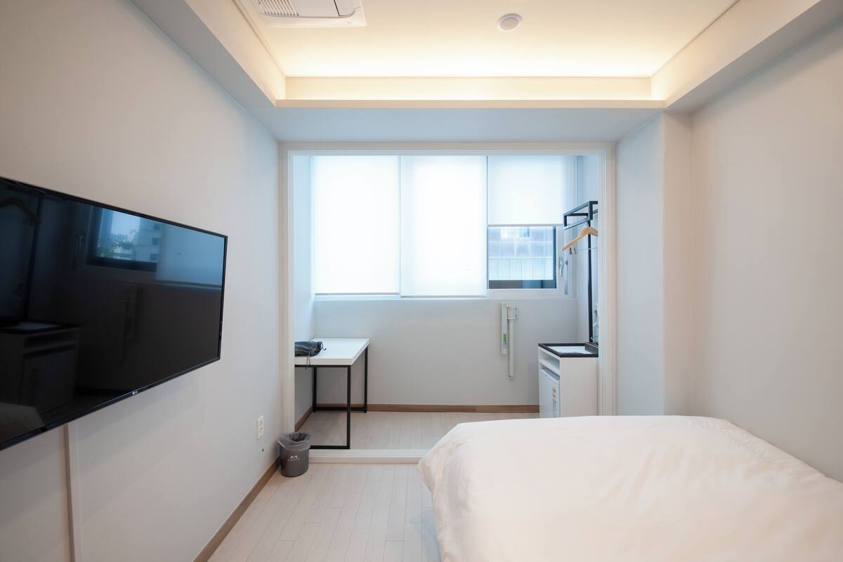 Quarto com cama, TV, escrivaninha e janela.
