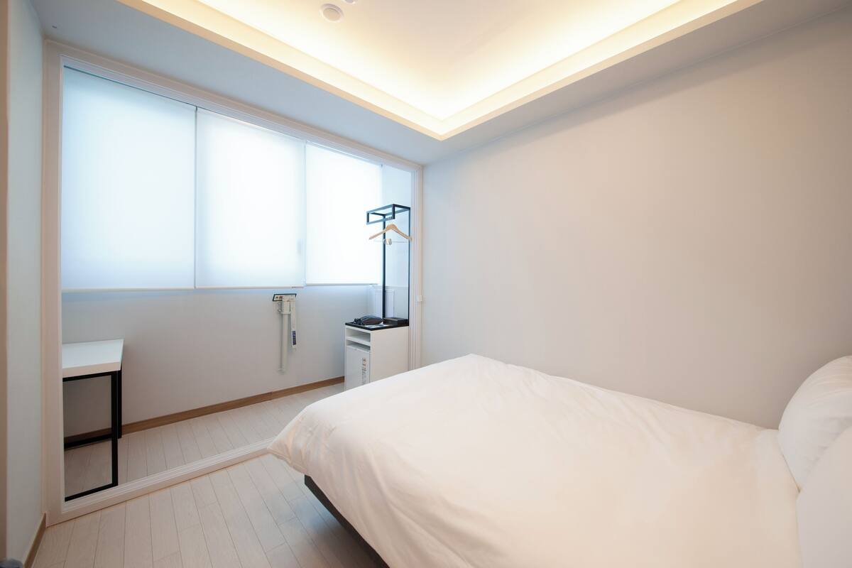 Quarto com cama, escrivaninha, cadeira e janela.