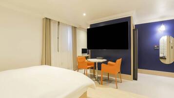 Quarto de hotel com cama, escrivaninha, duas cadeiras, televisão e espelho.