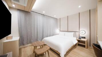 Quarto de hotel moderno com cama grande, mesa de cabeceira, cadeira e televisão.
