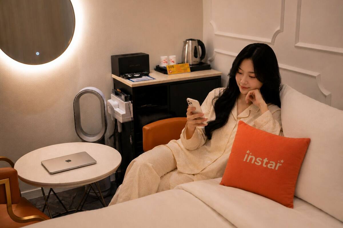 Quarto de hotel com cama, escrivaninha com um laptop, máquina de café e pequena mesa com um laptop.