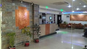 Um saguão de hotel com balcão de recepção, área de estar e painéis decorativos na parede.