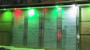 Um edifício com portões metálicos fechados, parede de tijolos vermelhos e toldo verde.