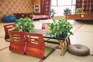 Um espaço com tatames, uma mesa baixa, cadeiras, um almofada e uma planta.