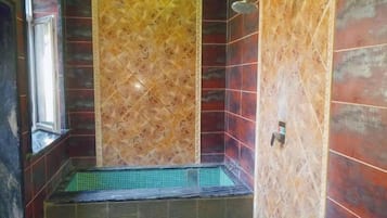 Casa de banho com chuveiro, janela e parede revestida a azulejos.