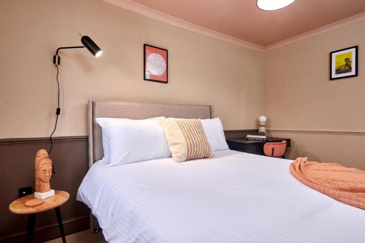 Quarto bem arrumado com cama, mesa de cabeceira, abajur e obras de arte na parede.