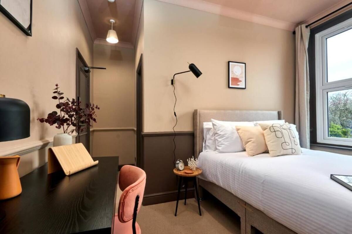 Quarto com cama, mesa de cabeceira, luminária, cadeira e janela.