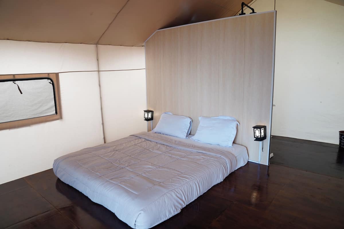 Quarto com cama, duas luminárias na parede, uma janela e cabeceira de madeira.