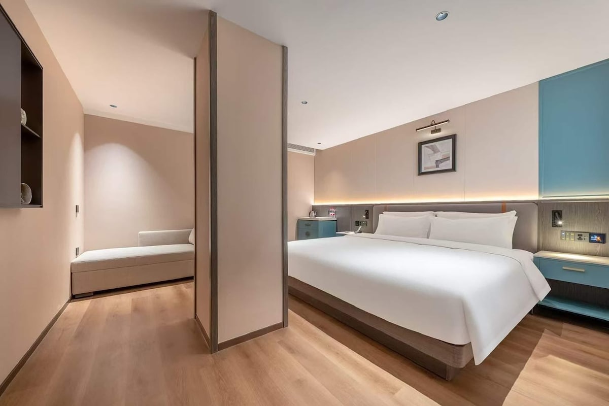 Quarto de hotel moderno com uma cama grande, mesas de cabeceira, escrivaninha embutida e TV na parede.
