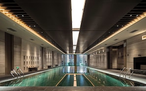Piscina interior moderna com um corredor central, rodeada por paredes com iluminação embutida e um claraboia.