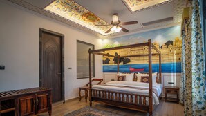 Uma cama de dossel com ventoinha no teto, um mural grande, um banco de madeira e uma mesa pequena.
