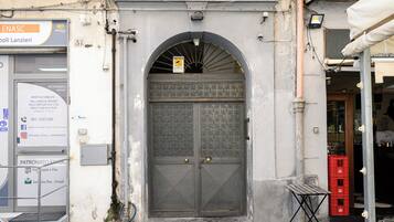 Entrada de um edifício com porta de metal, placa com o logotipo ENASC e escadaria que leva à entrada.