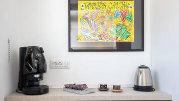 Uma bancada de cozinha com uma cafeteira, uma chaleira e uma obra de arte colorida emoldurada.