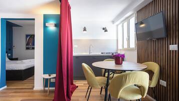 Quarto moderno com cama, área de jantar com cadeiras, cozinha com pia e televisão fixada na parede.