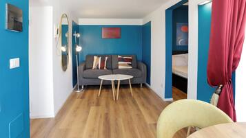 Uma sala de estar moderna com um sofá cinza, uma mesa redonda branca e uma parede azul decorativa.