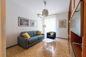 Uma sala de estar moderna com um sofá cinzento, uma poltrona azul e uma mesa de centro redonda.