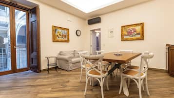 Uma sala de jantar com mesa de madeira e cadeiras brancas, um sofá e uma pequena mesa lateral.
