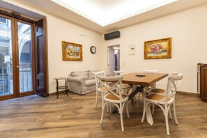 Uma sala de jantar com mesa de madeira e cadeiras brancas, um sofá e uma pequena mesa lateral.