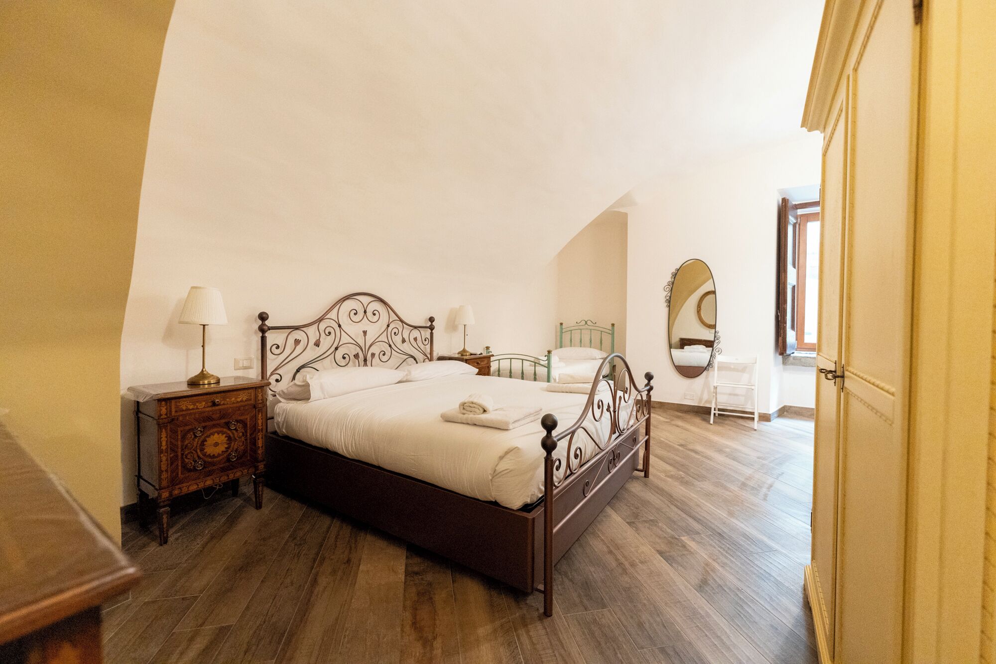 Quarto com cama de madeira, duas mesas de cabeceira com luminárias, um espelho e um guarda-roupa.